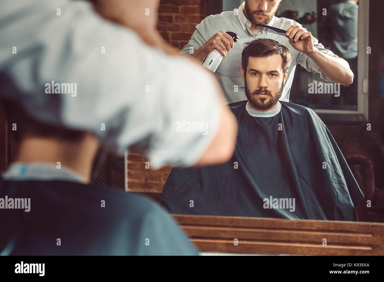 Young handsome barber making haircut of attractive man in barbershop ...