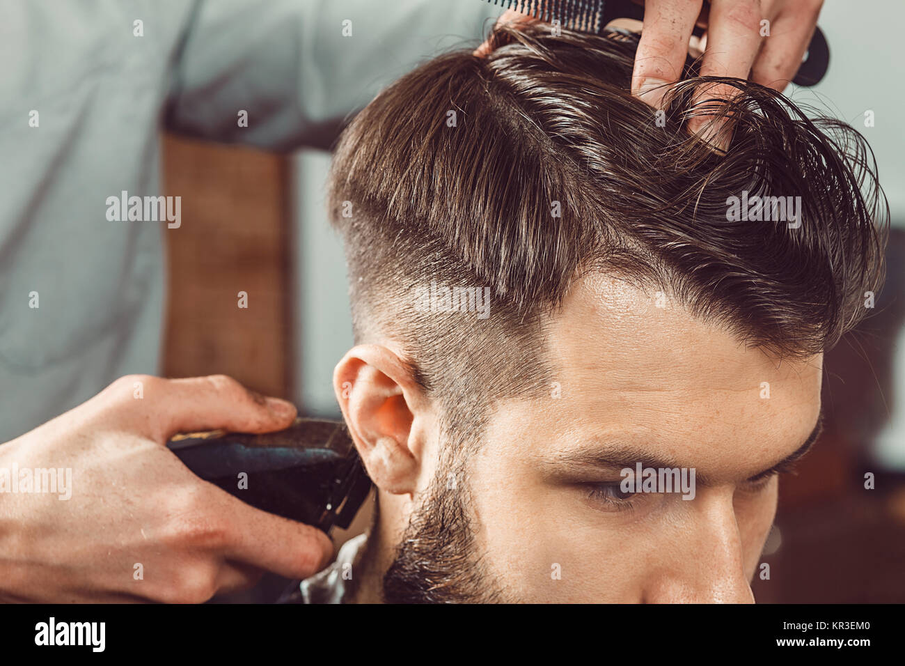 The hands of young barber making haircut to attractive man in ...