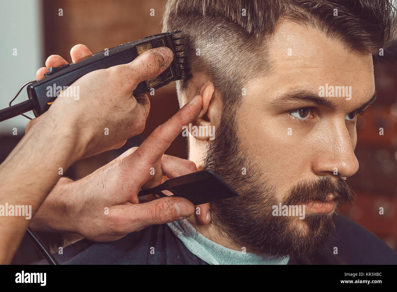 The hands of young barber making haircut to attractive man in ...