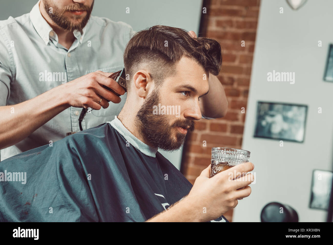 Young handsome barber making haircut of attractive man in barbershop ...