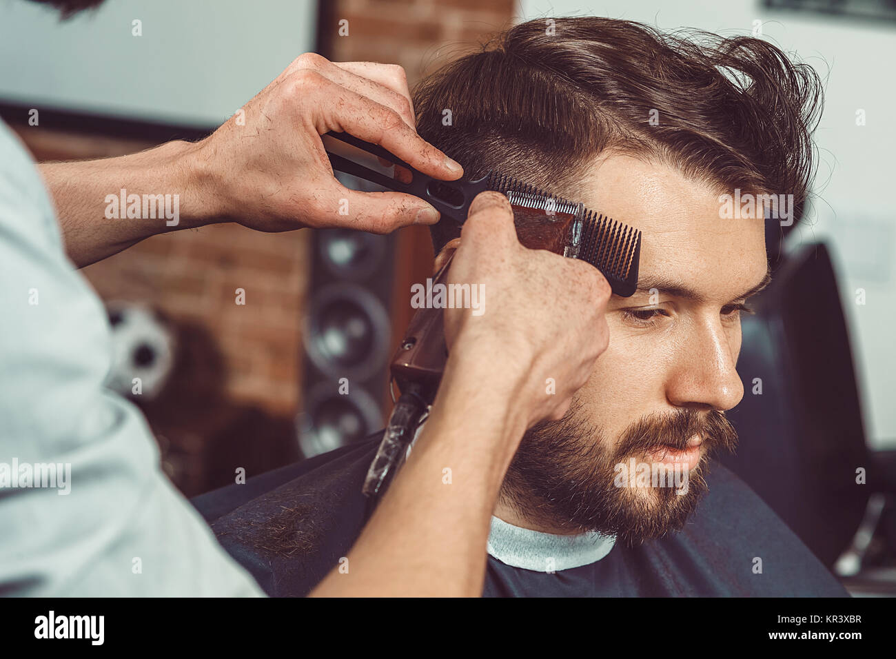 The hands of young barber making haircut to attractive man in ...