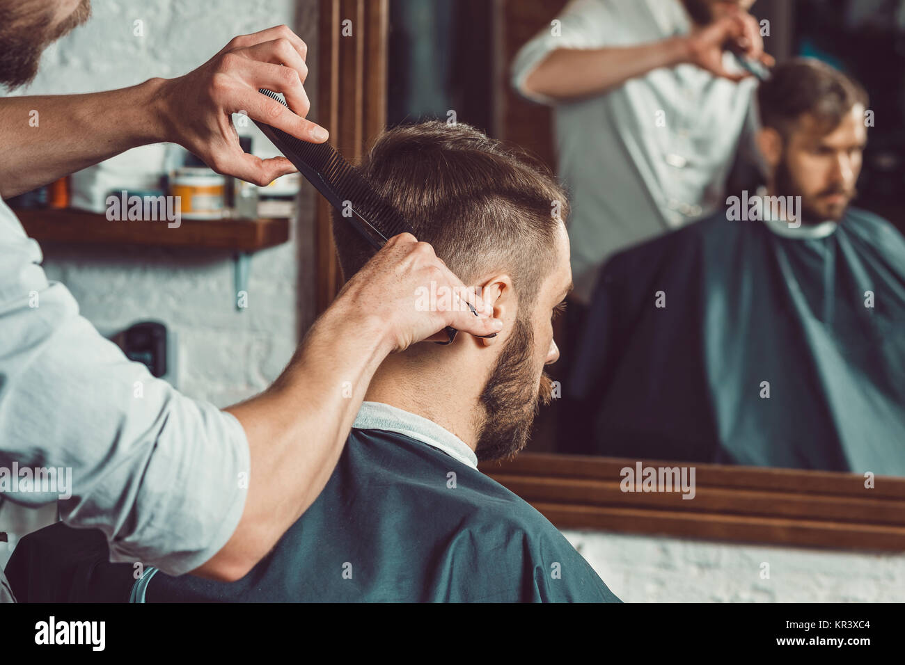 The hands of young barber making haircut to attractive man in ...