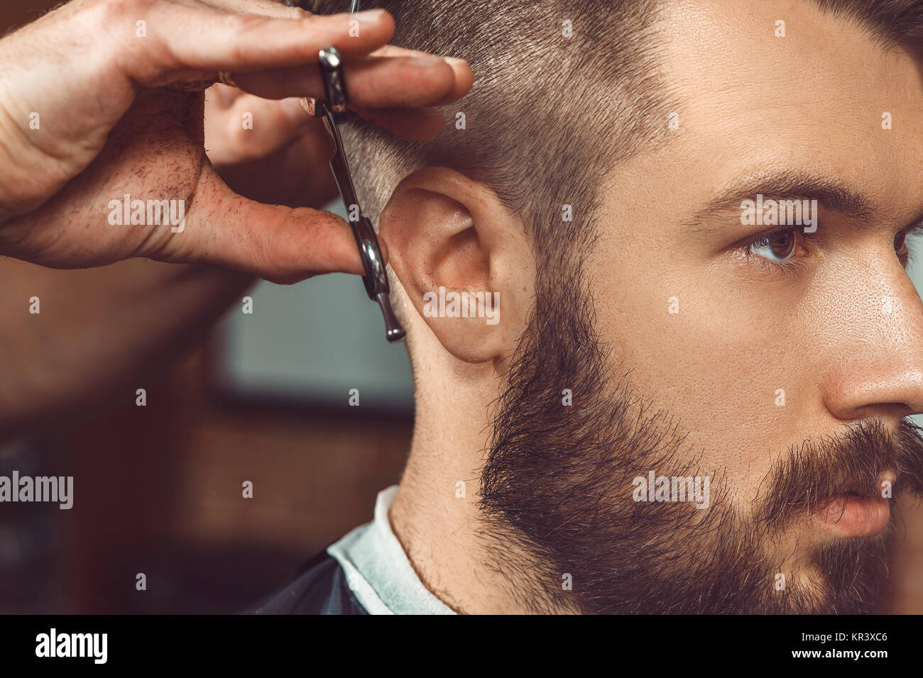 The hands of young barber making haircut to attractive man in ...