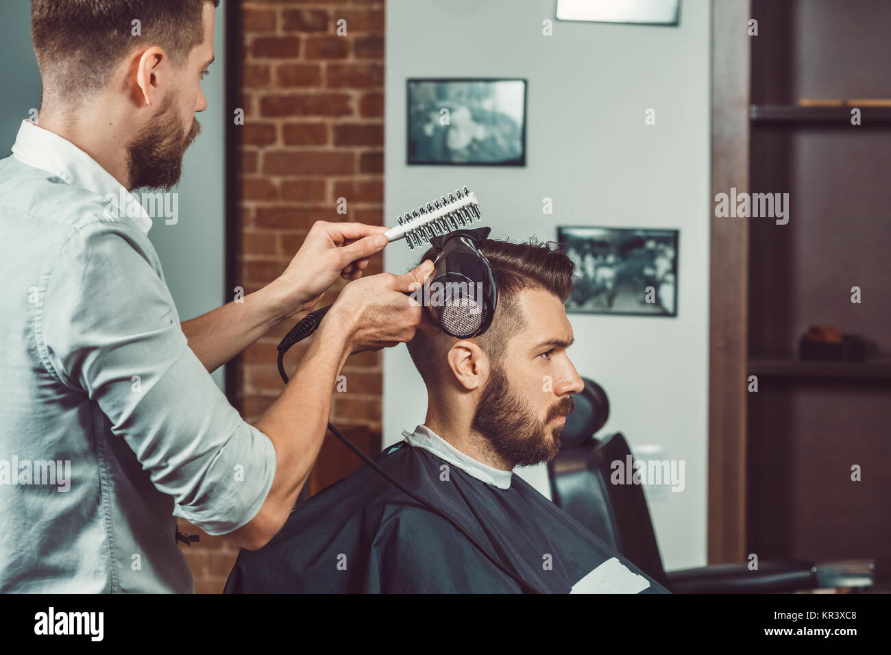 Young handsome barber making haircut of attractive man in barbershop ...