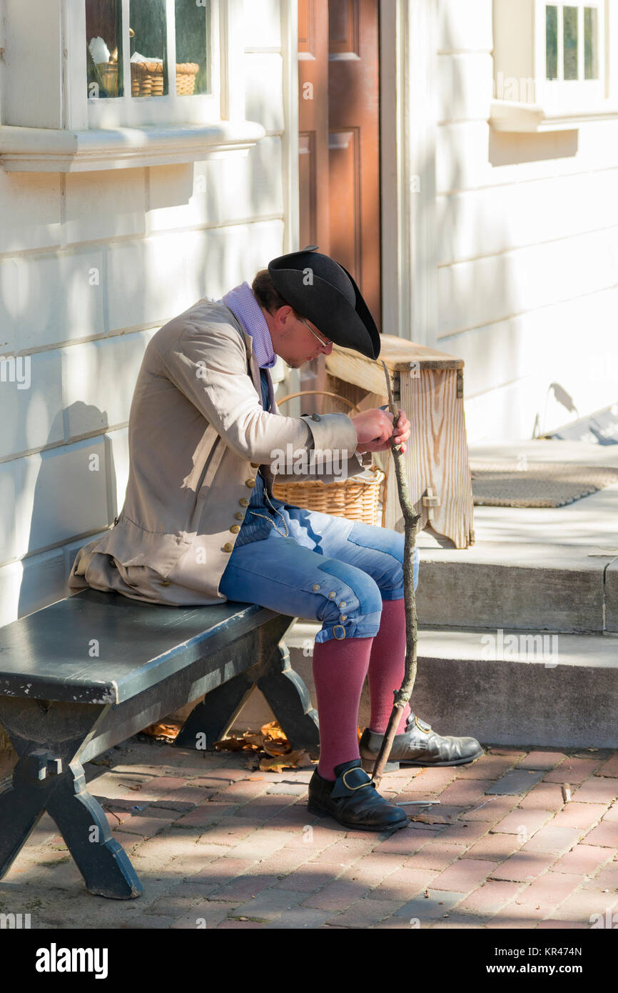 Costumed interpreter seated on bench along Duke of Gloucester Street ...