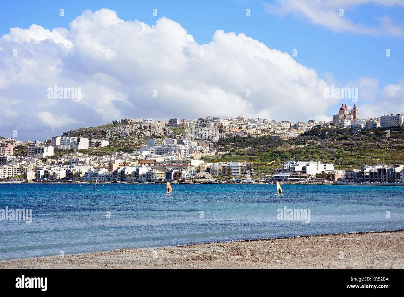 View of the sandy beach with town buildings across the bay, Mellieha ...