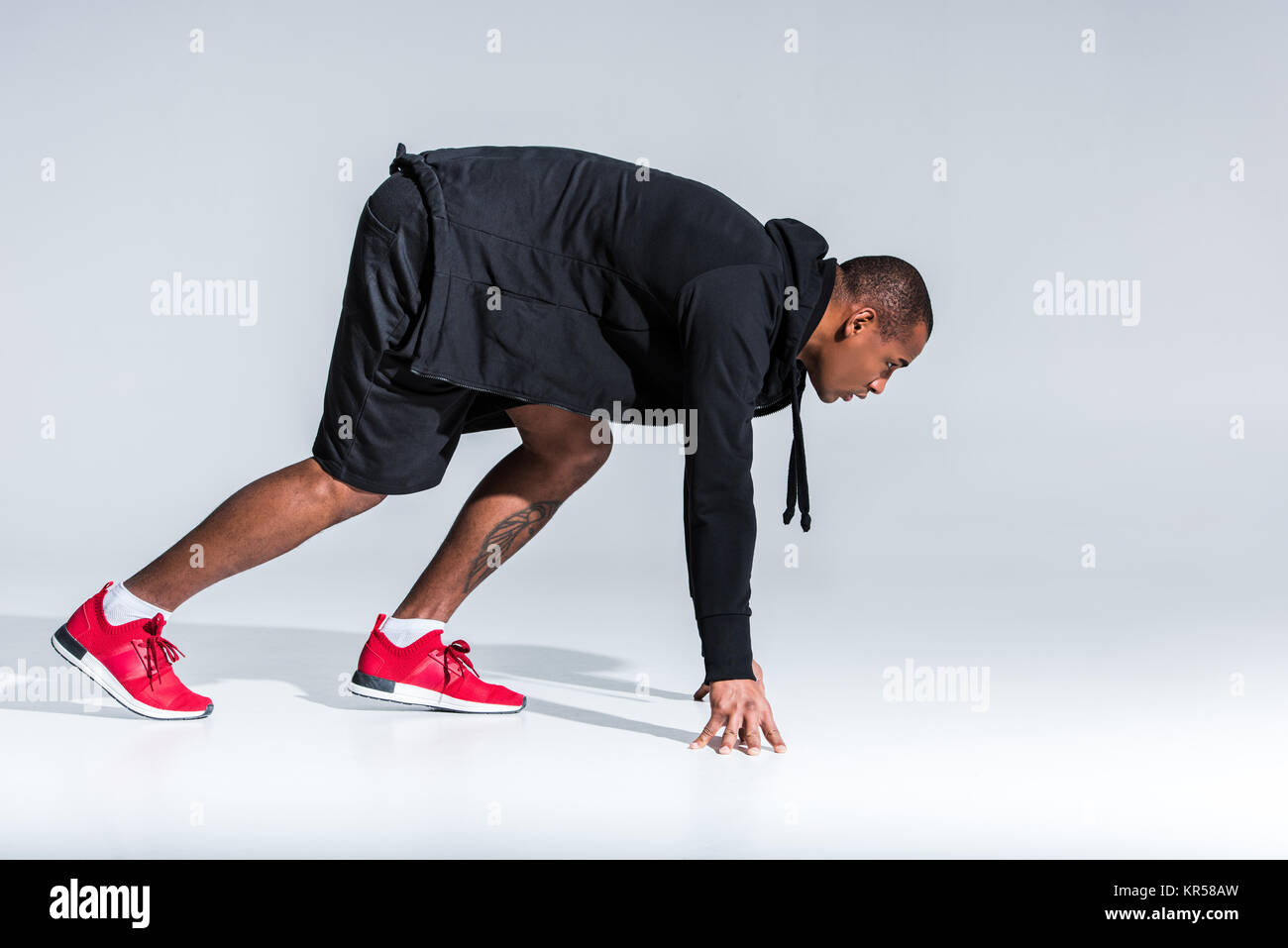 side view of young african american sportsman in hoodie ready to run on ...