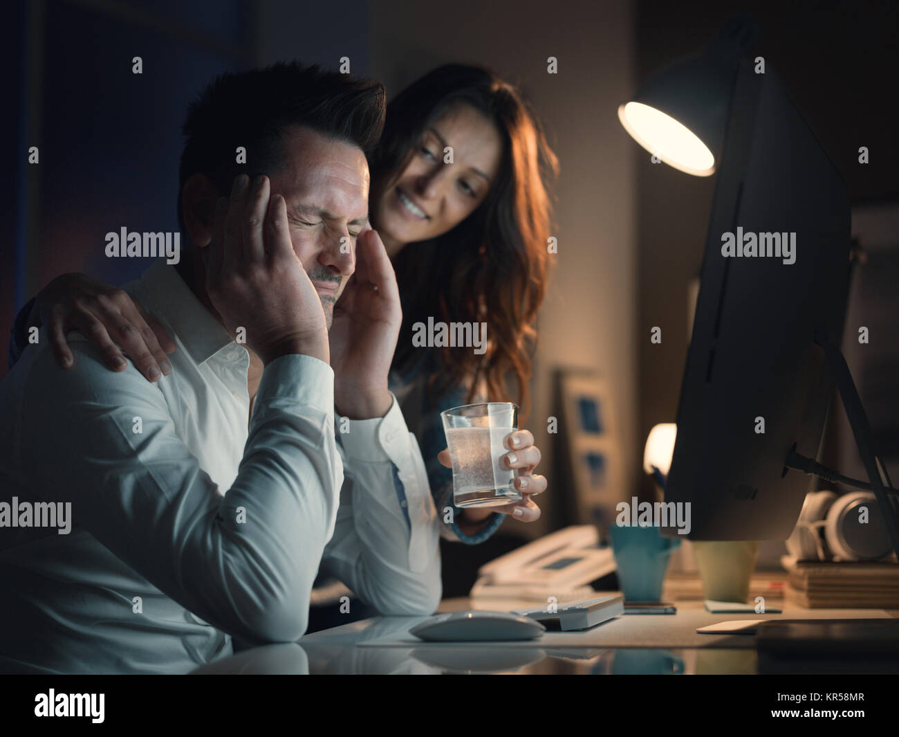 Man working with his computer and having a bad headache, his wife is ...