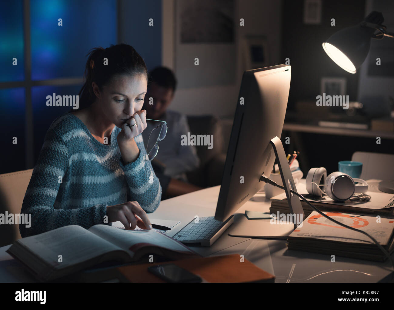 Young woman studying at home late at night, she is reading a book and ...