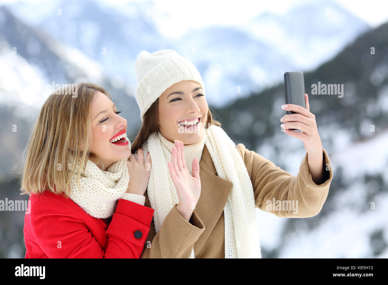 Two happy tourists having a video call with a smart phone in winter ...