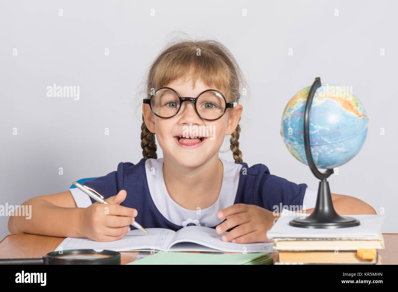 Happy first grader sits at a table in the classroom, with his mouth ...
