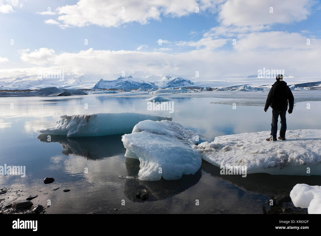 Rear view of person standing on ice sheet on glacial lagoon with ...