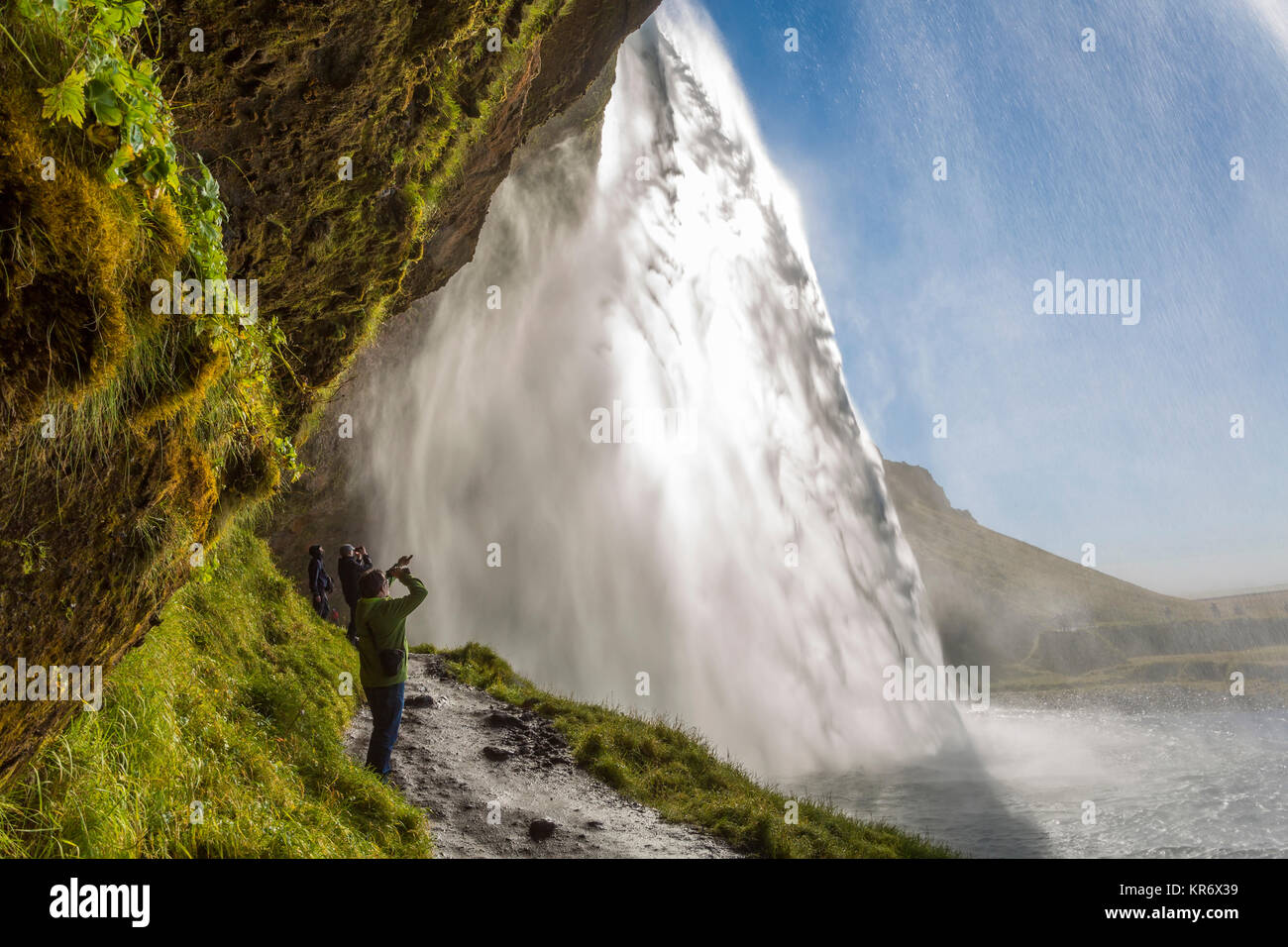 People standing on a narrow path underneath a waterfall cascade over a ...