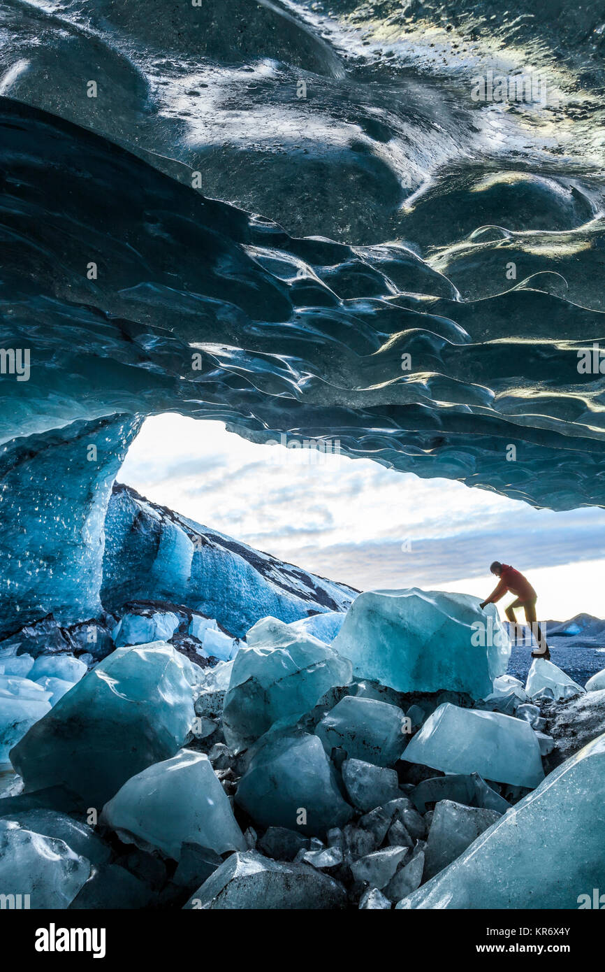 Side view of person climbing up on ice rock at the entrance to a ...