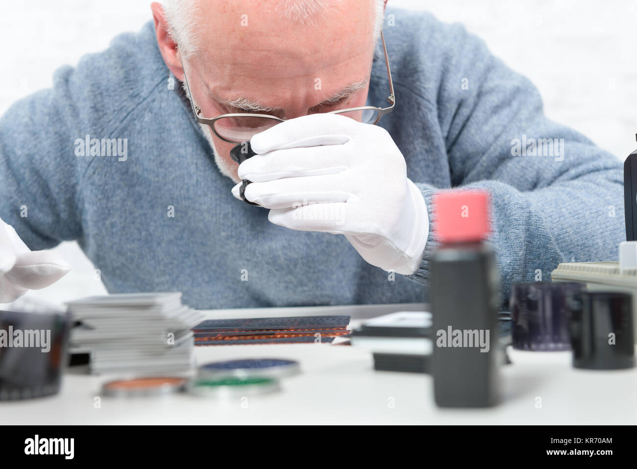 a man photographer looking at negative film with a magnifying glass ...