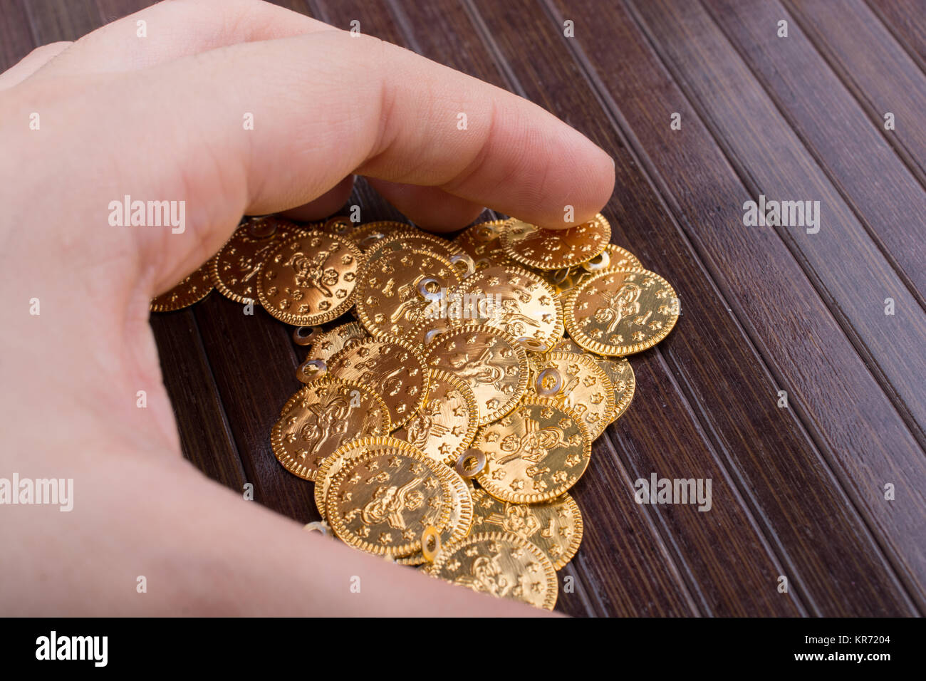 Plenty of fake gold coins in hand on wooden background Stock Photo - Alamy