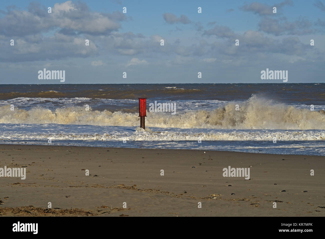 waves breaking around a marker post on a on sandy shore Eccles-on-Sea ...
