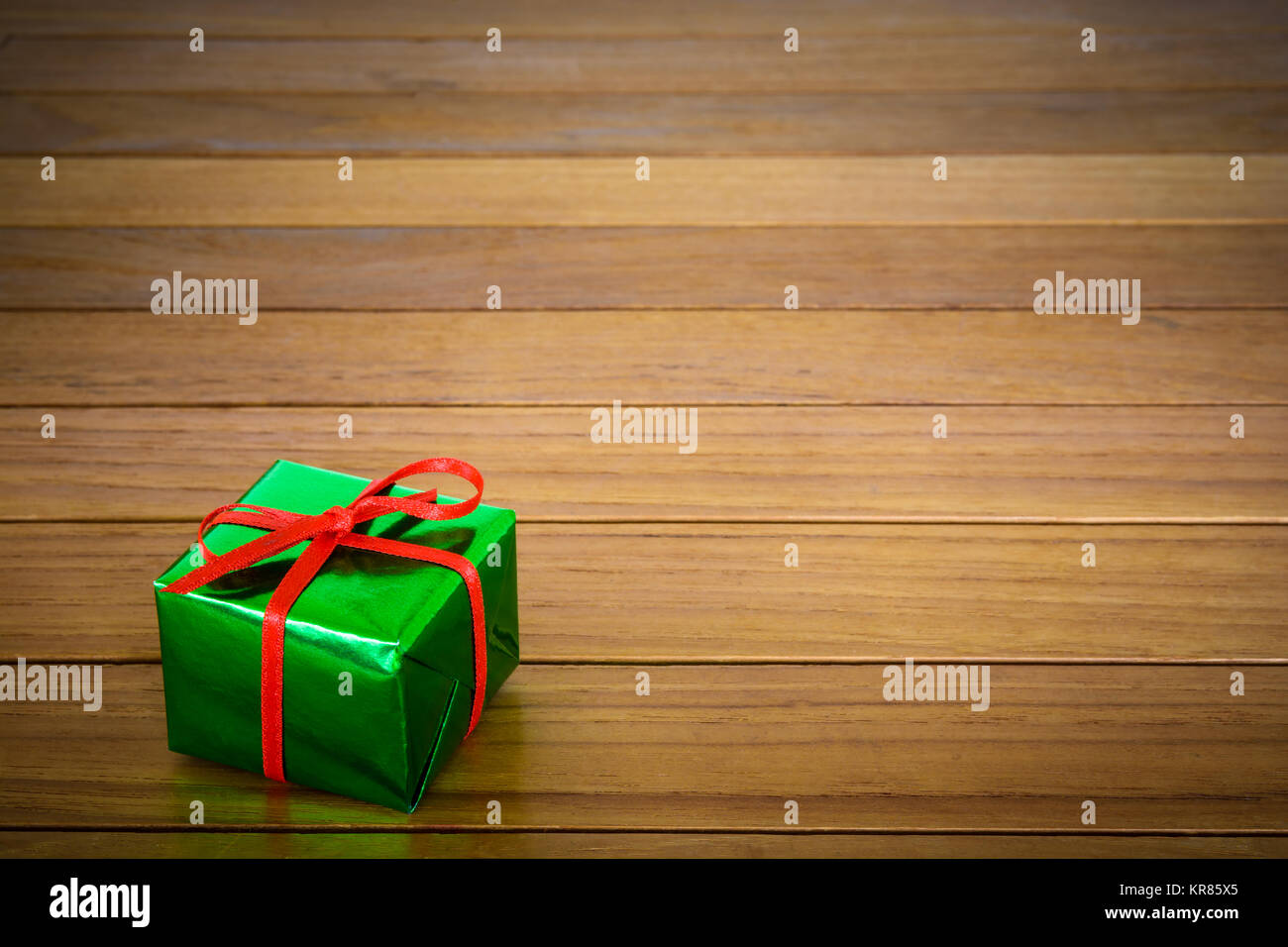 Metallic green gift package with red ribbon on a wooden background ...