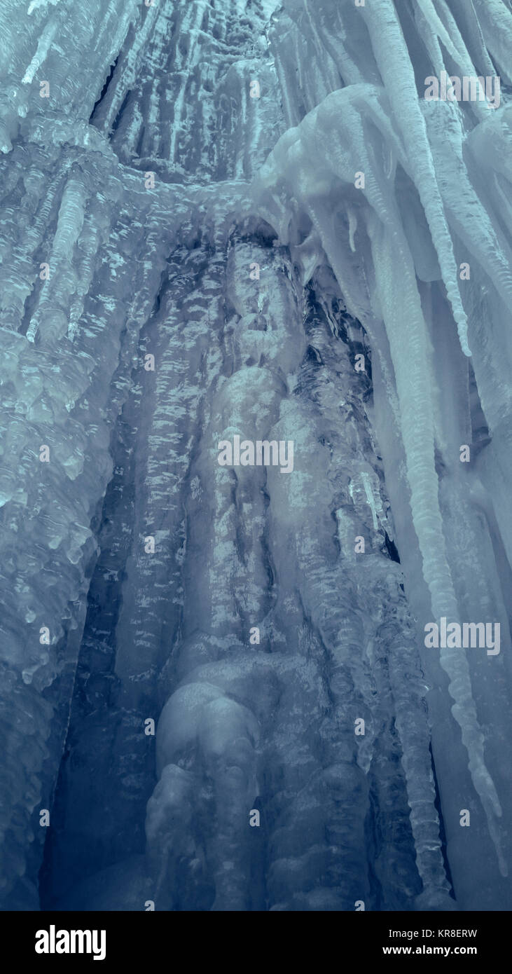 Vertical slippery steep ice wall with long icicles in a cavern. Frozen ...