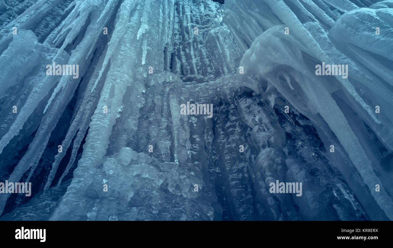 Vertical slippery steep ice wall with long icicles in a cavern. Frozen ...