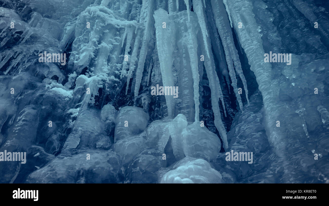 Vertical slippery steep ice wall with long icicles in a cavern. Frozen ...