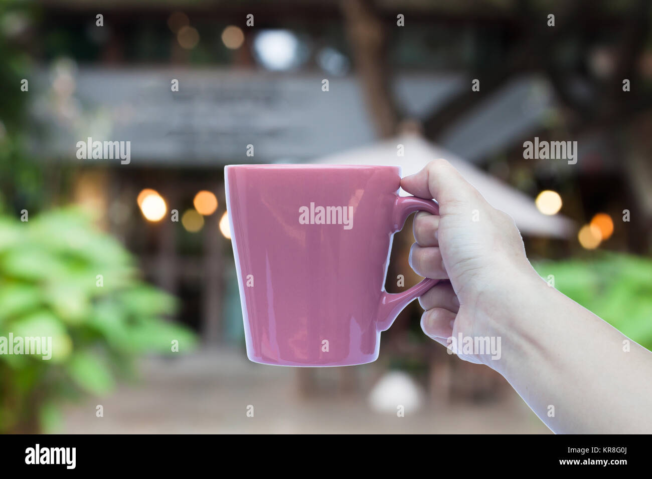 Woman hand holding coffee mug with cafe background Stock Photo - Alamy