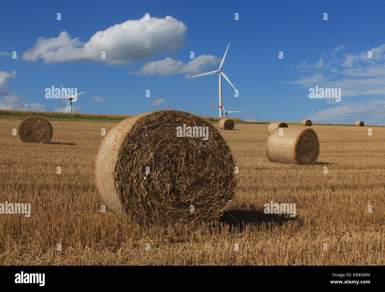 stubble with hay bales and wind turbines in the background against blue ...