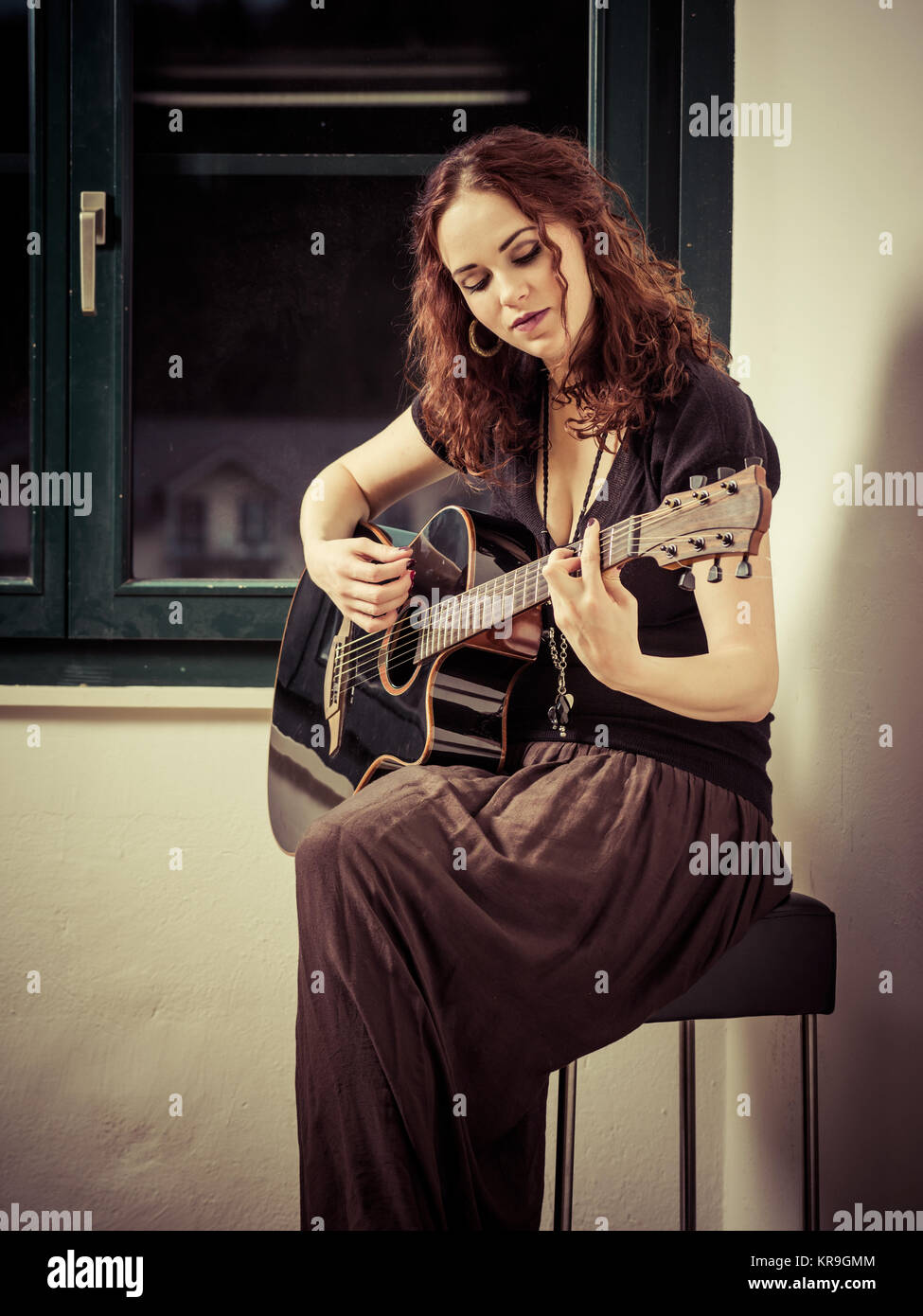 Young woman playing guitar by the window Stock Photo - Alamy