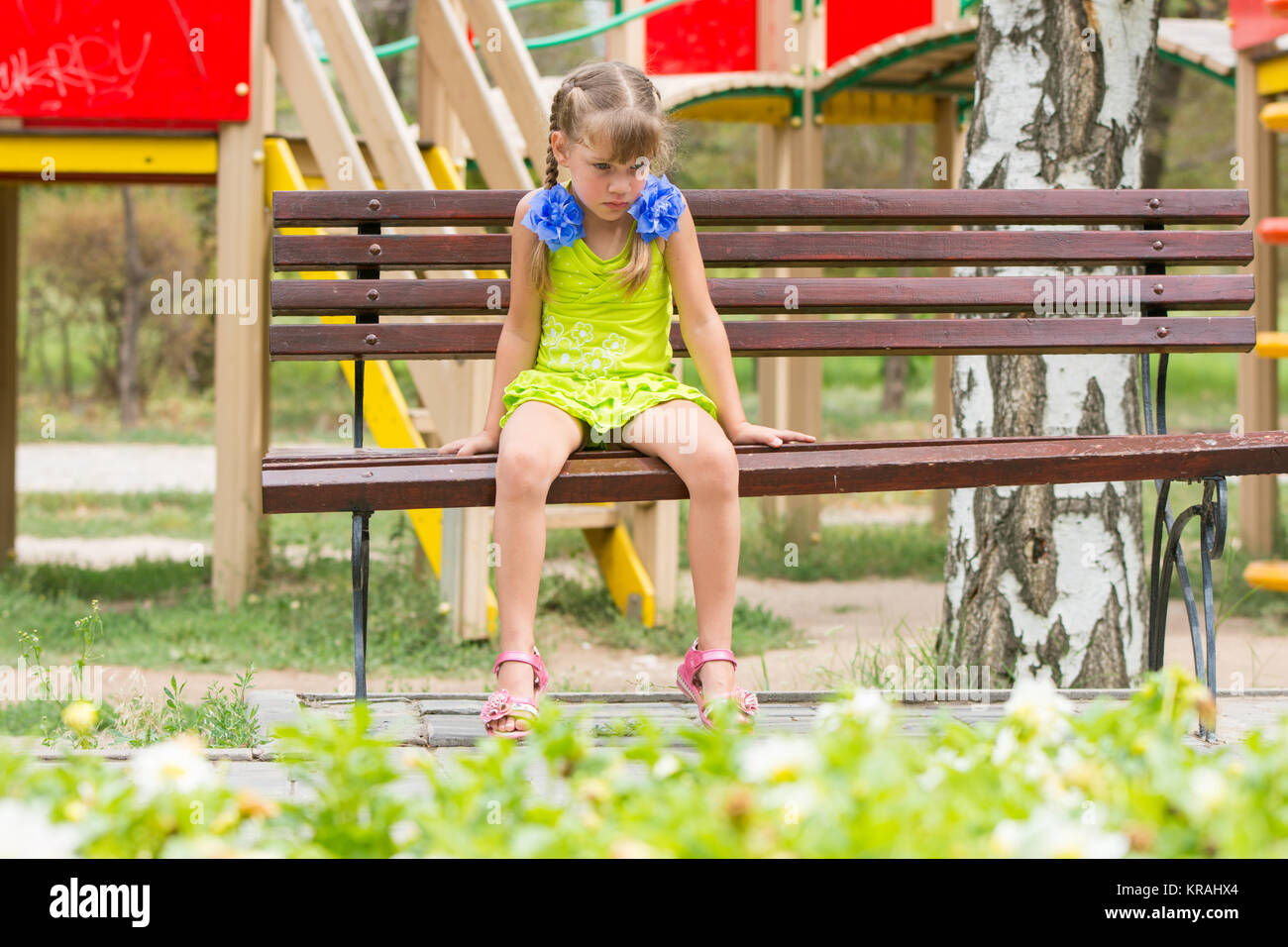 Crying girl sitting on the bench on the background of the playground ...