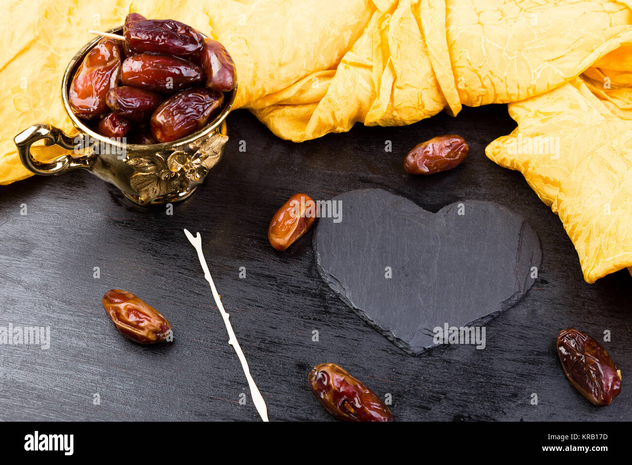 Dry fruit dates in golden cup near slate black heart. Copy space ...