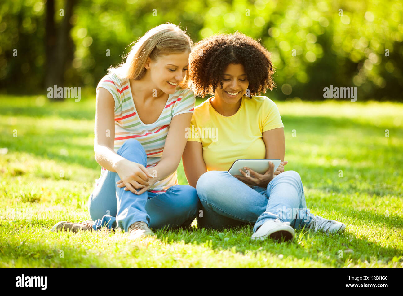 Two young women using tablet in park Stock Photo - Alamy