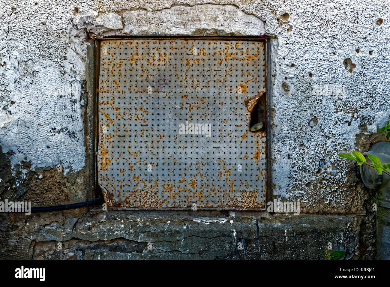 rusty door with circular holes in it and a pipe coming out. attached to ...