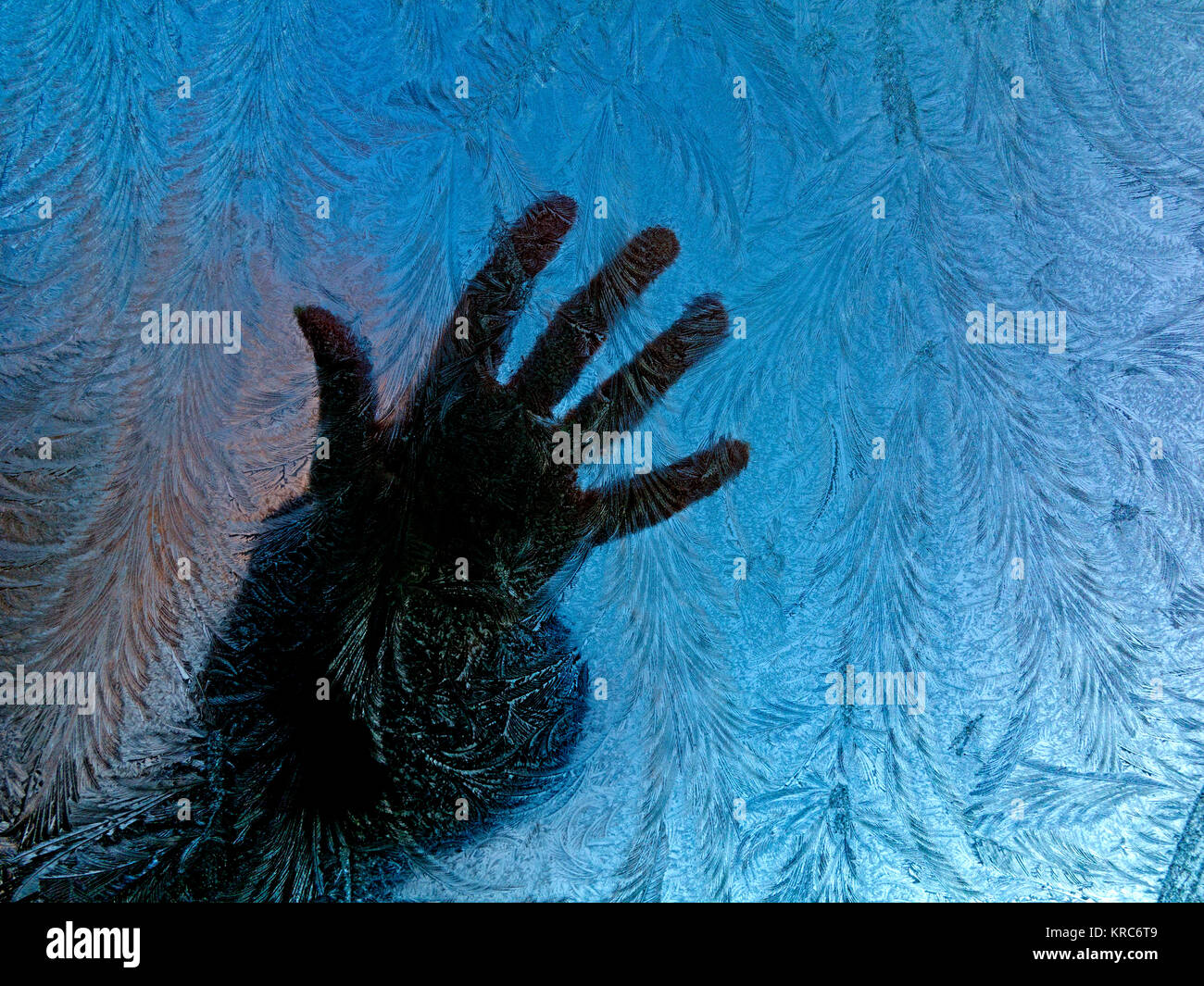 Ice formation on a car windscreen with a silhouetted hand out side ...