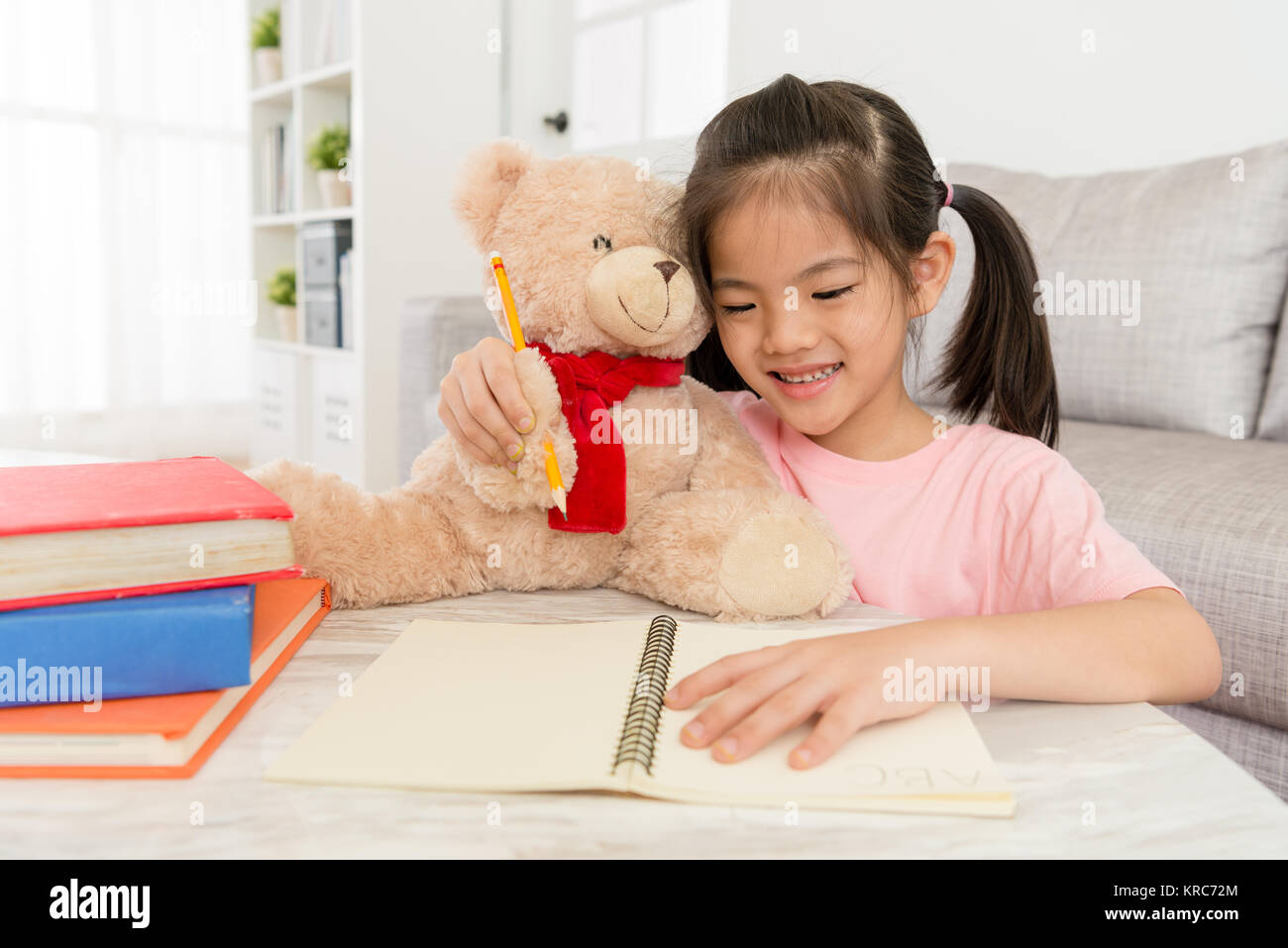 cheerful smiling little girl doing homework with her teddy bear toy at ...
