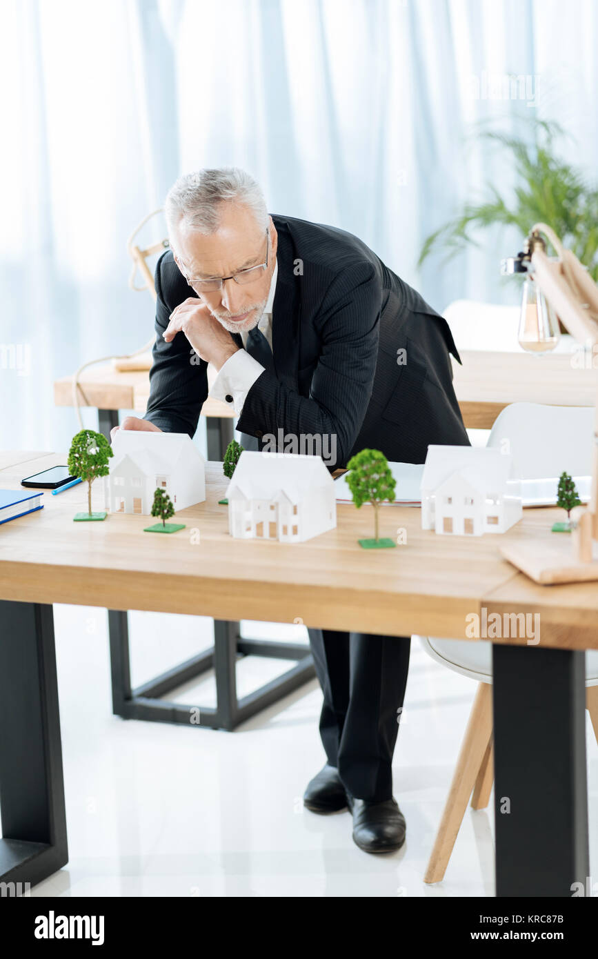 Concentrated experienced realtor looking at the miniature houses and ...