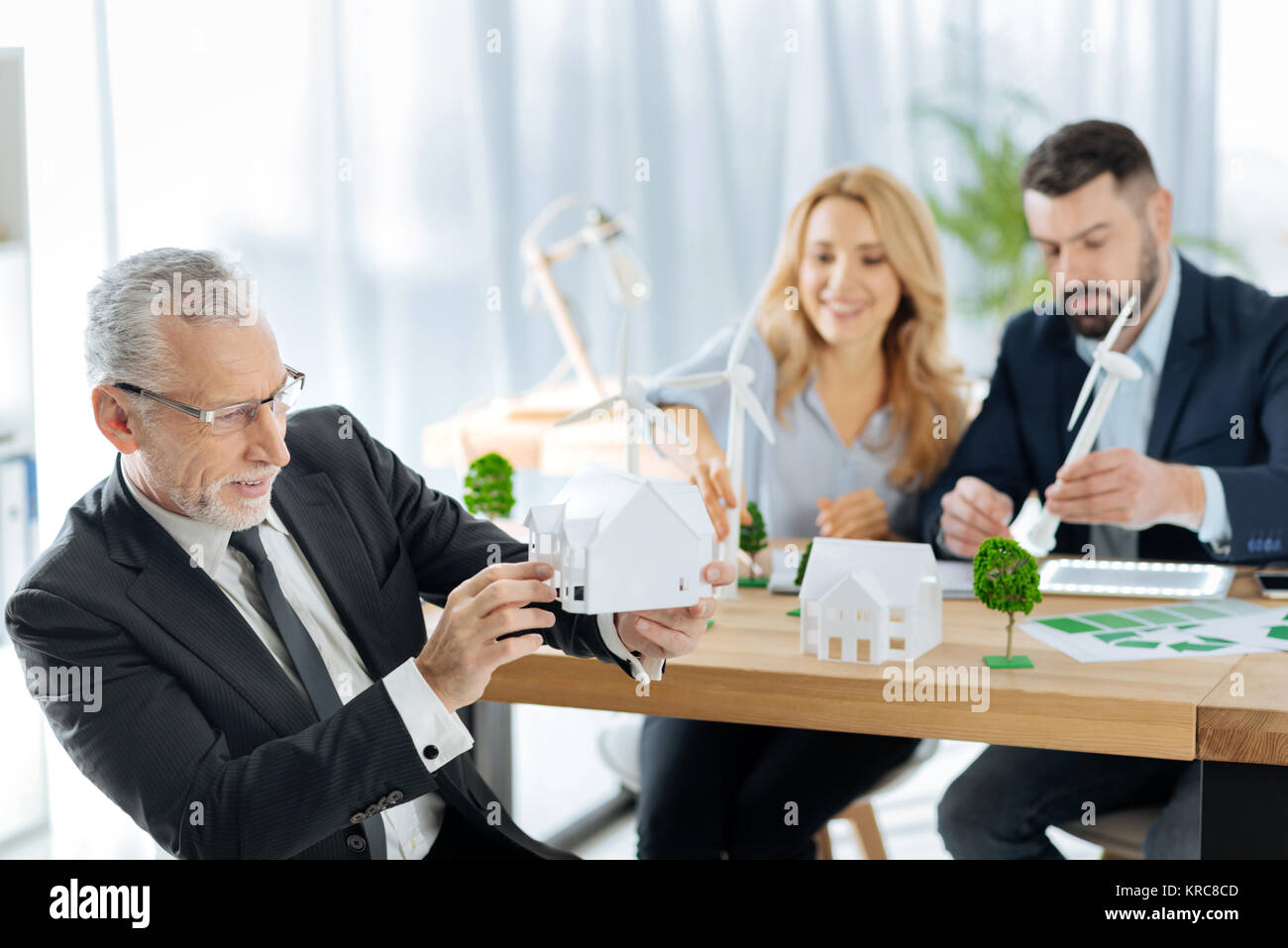 Curious engineer holding a miniature house while his colleagues sitting ...