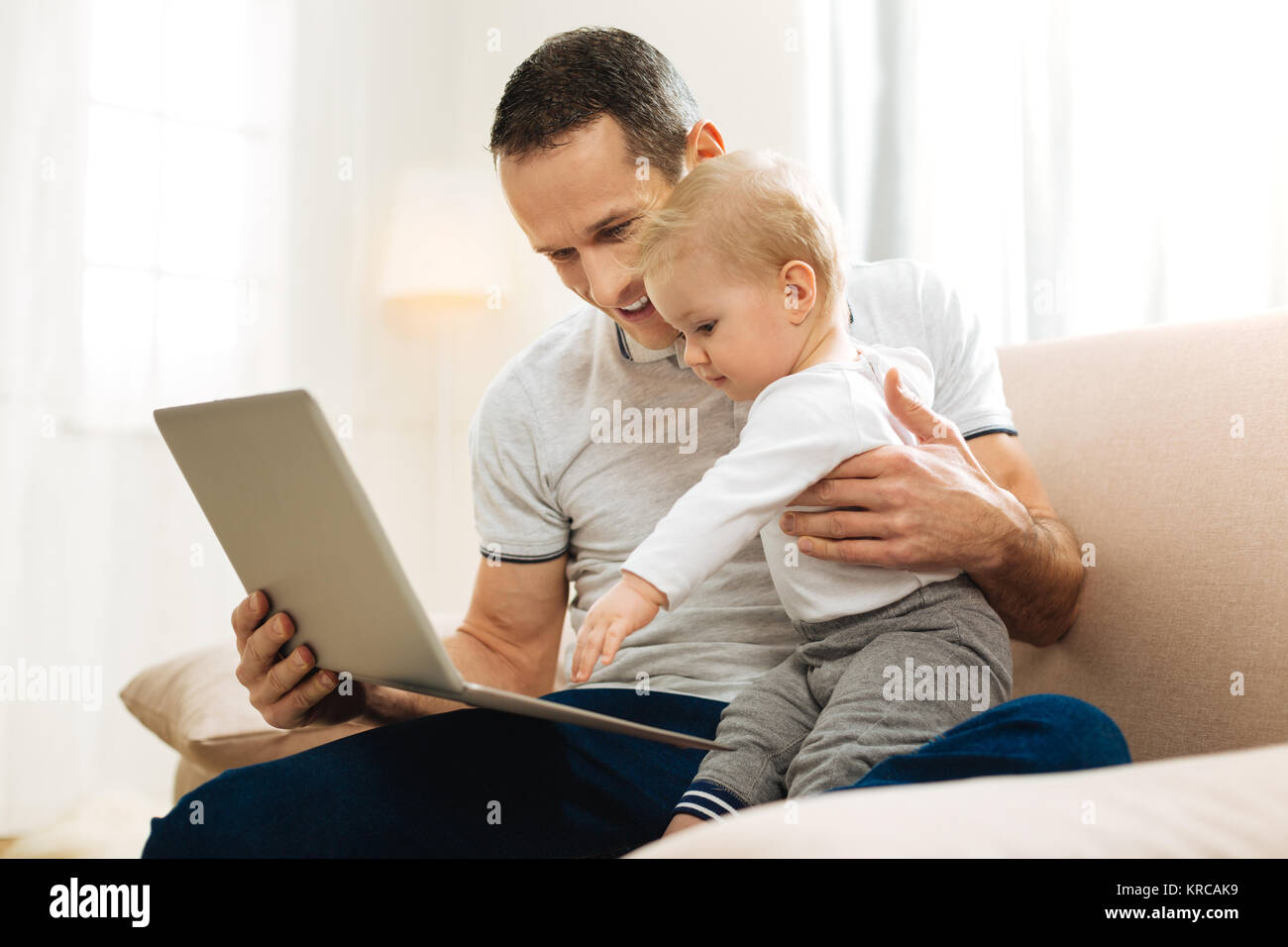 Kind positive father sitting with his child and looking at the gadget ...