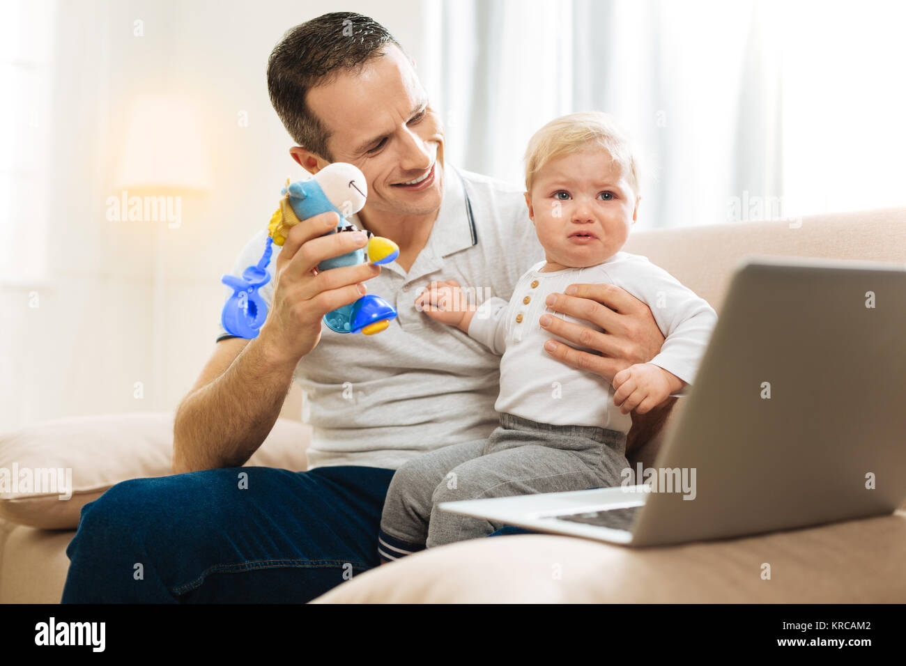 Kind attentive father showing a toy to his crying baby and smiling ...