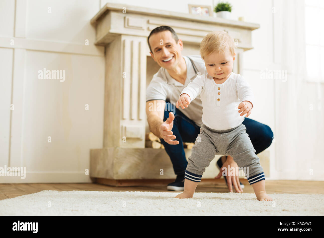 Happy baby trying to stand up while a cheerful father being ready to ...