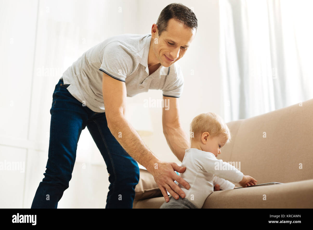 Adorable kind father helping his baby to stand near the sofa Stock ...