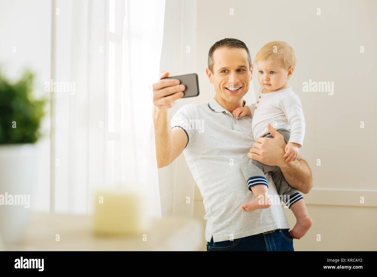 Kind father taking photos with a baby while standing near the window ...