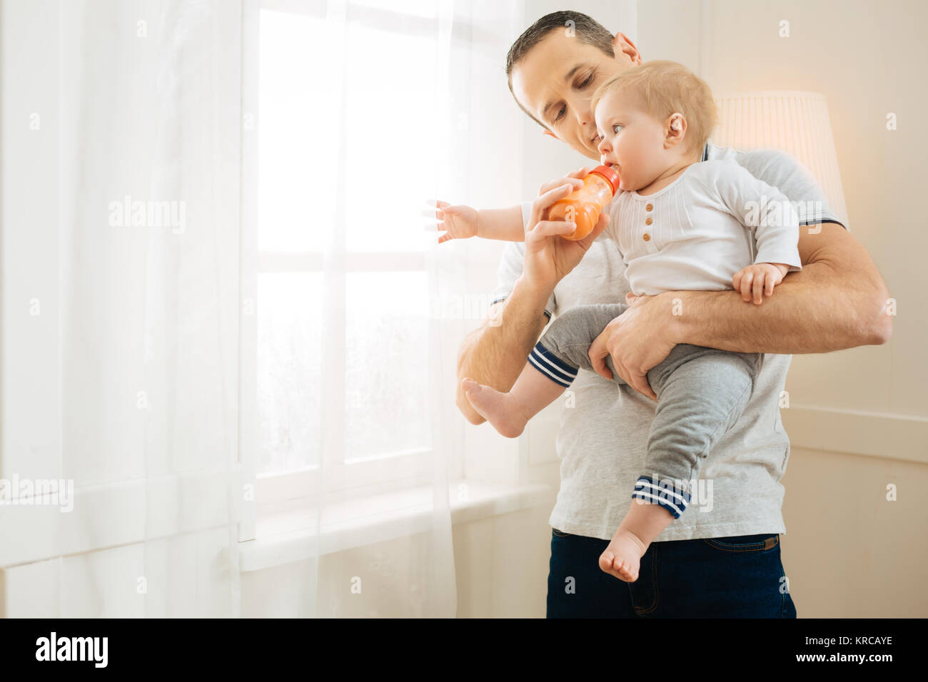 Attentive responsible father feeding his baby and looking concentrated ...