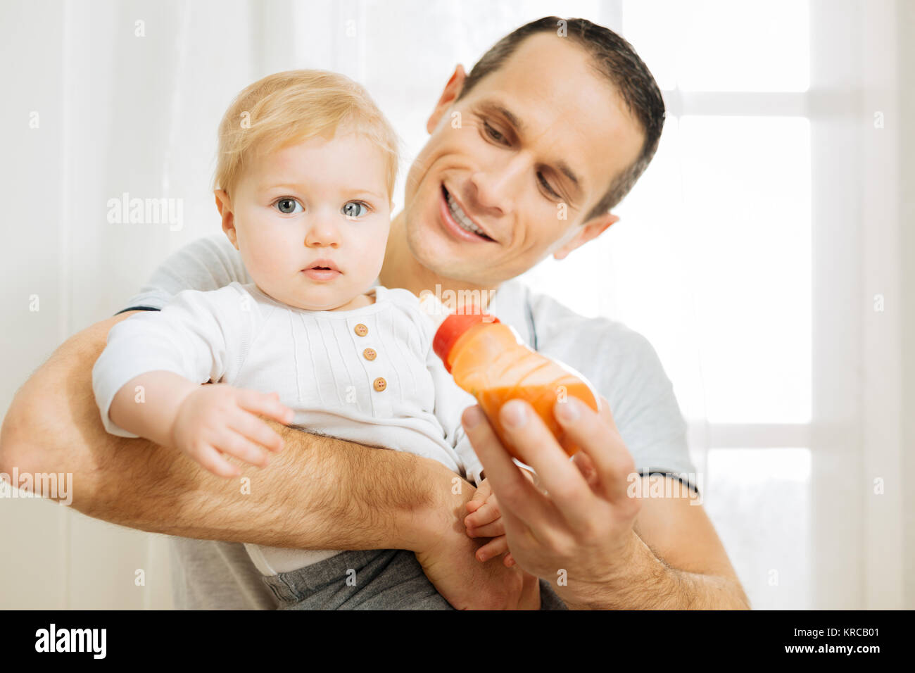 Attentive responsible father offering his child a bottle and smiling ...