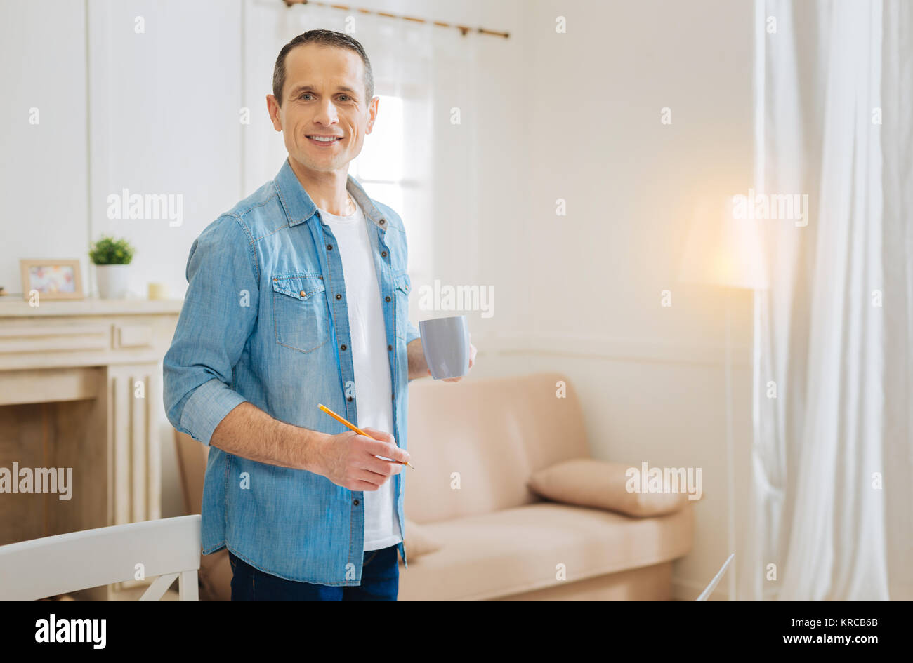 Positive cheerful engineer holding a pencil while drinking tasty tea ...