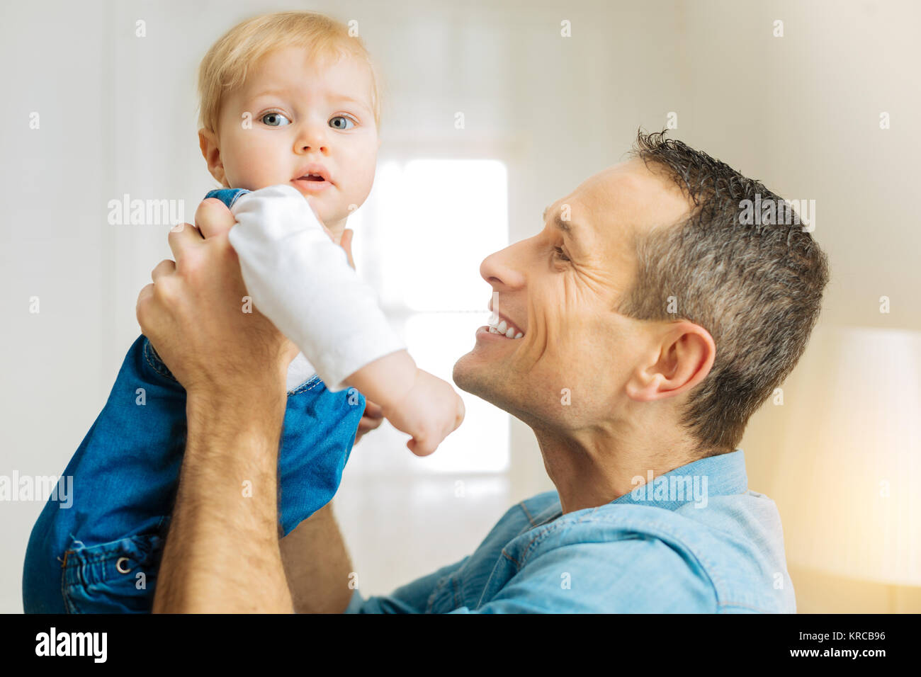 Cheerful emotional father looking attentively at his baby and feeling ...