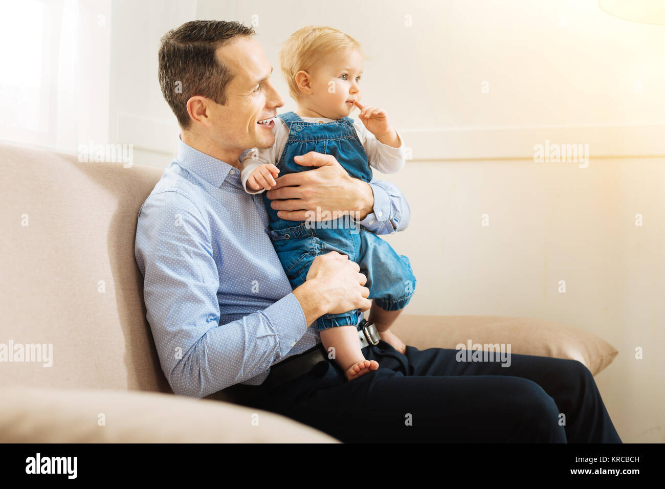 Positive young father watching a nice film while holding his baby Stock ...