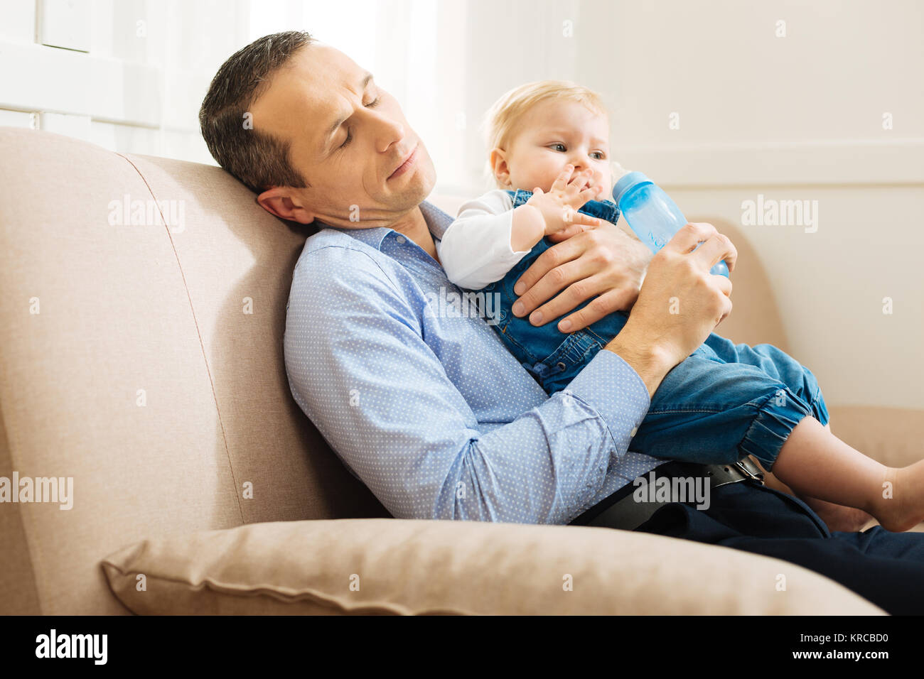 Tired father falling asleep while sitting with his active baby Stock ...