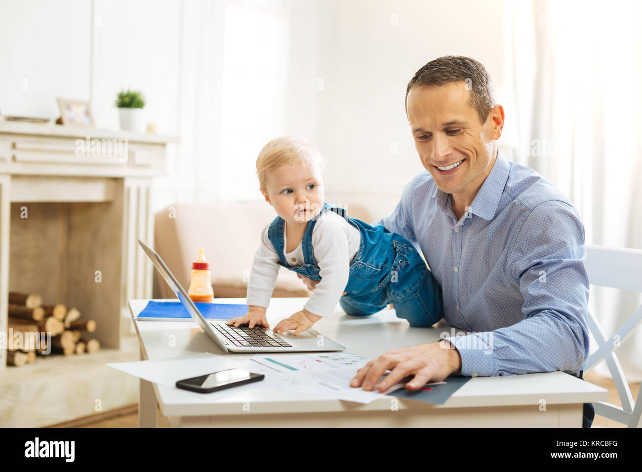 Lovely baby touching a laptop on the table while helping his father ...