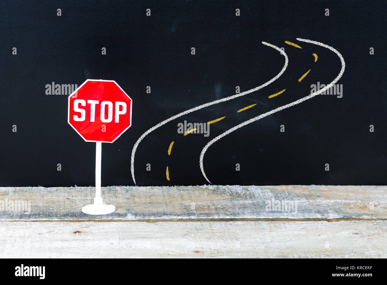 Mini STOP sign in front of curved road, hand drawing over chalkboard ...