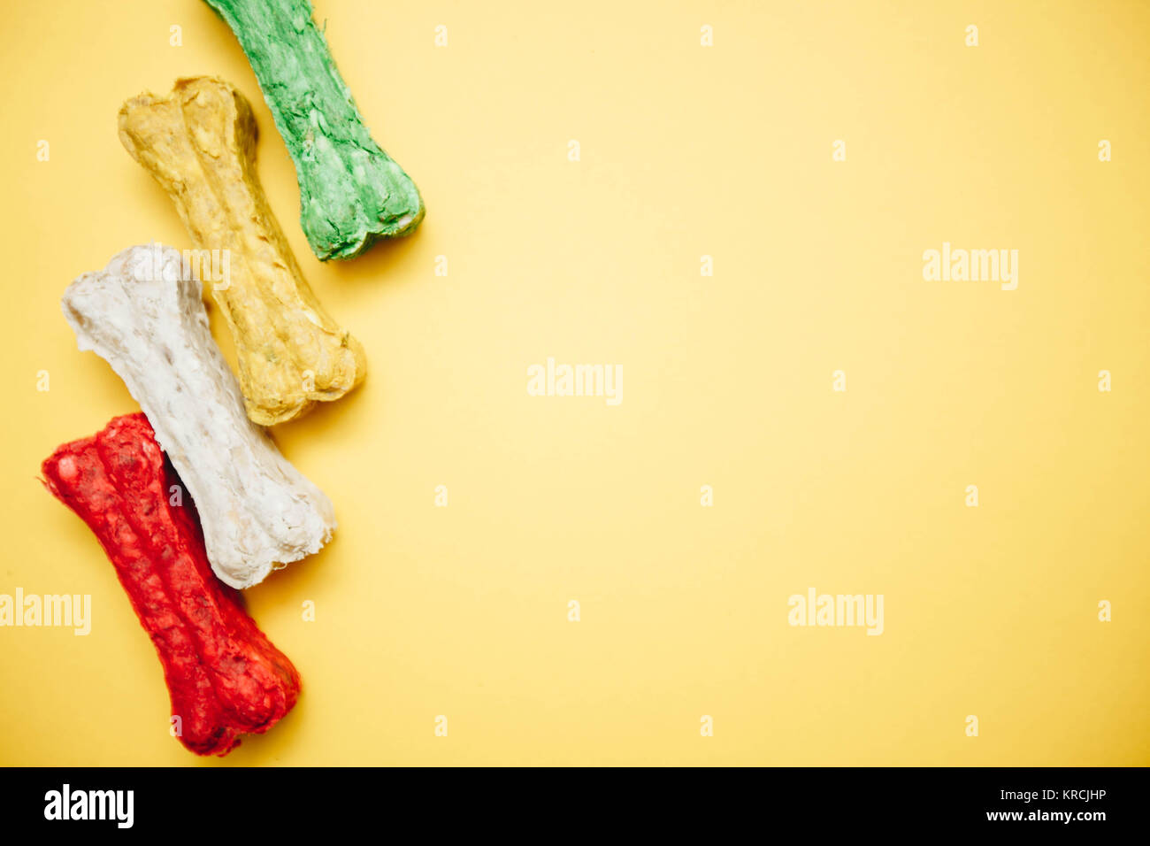 Yellow one-color background with colored dog bone snacks in a row ...